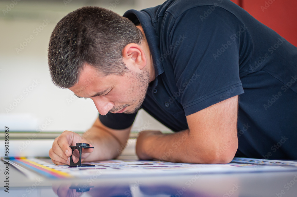 Young man in the process of printing used color scales and loupe and ...