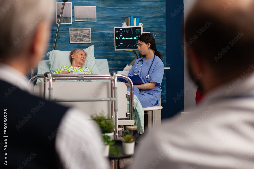 Elderly woman lying in hospital clinic bed talking to nurse about ...