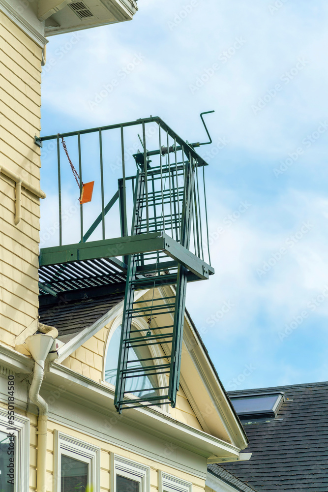 Dark metal fire escape ladder on exterior facade of beige slatted wood ...