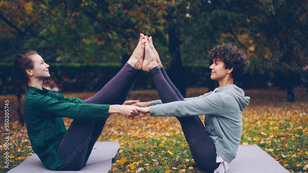 Attractive girls are doing yoga exercises in pair holding hands and ...