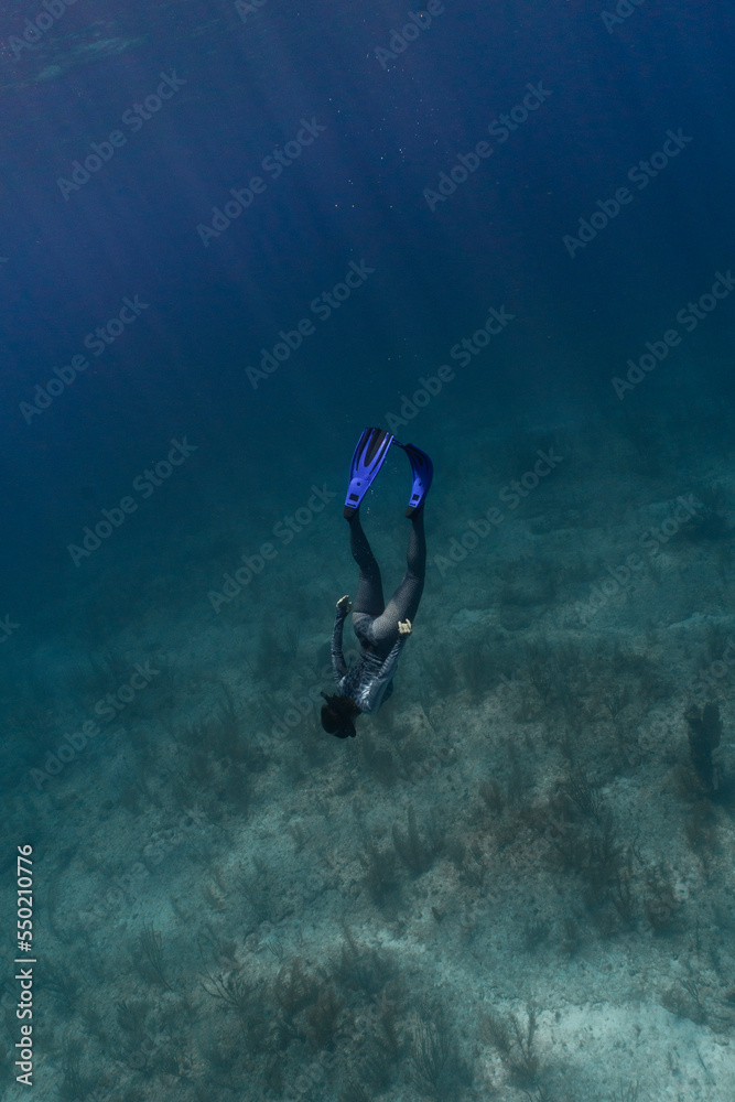 Vertical underwater shot of woman free diving to the bottom of the ...