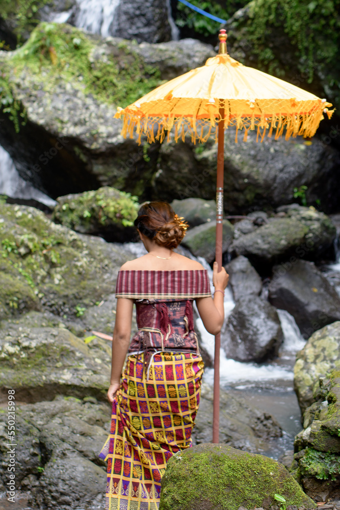 Girl in classic Balinese clothes pose at the Yeh Labuh waterfall, back ...