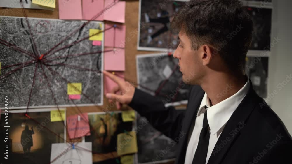Detective looking at board with fingerprints, photos, map and clues ...