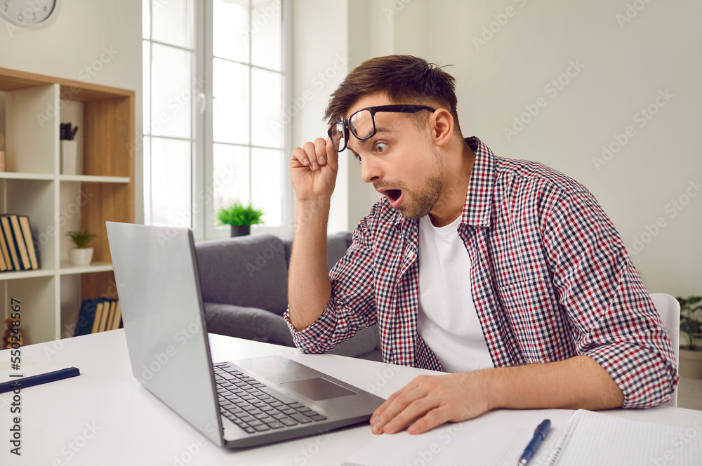Man who works at home is looking at laptop screen with shocked ...
