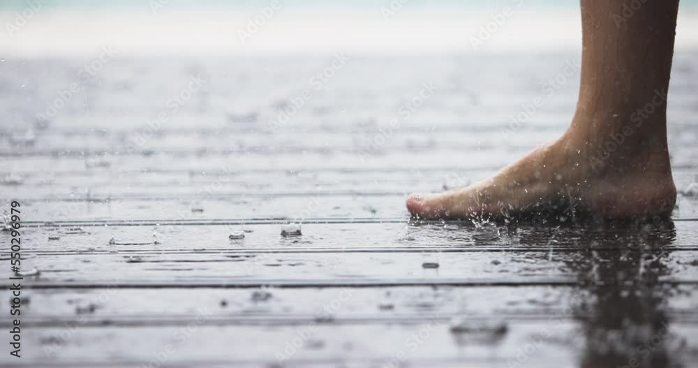 Women's barefoot covered in droplets of heavy rain in close-up ...