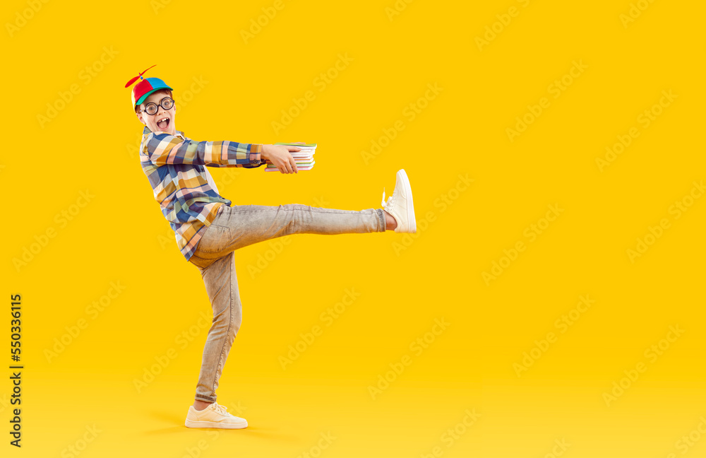 Cheerful preteen boy nerd is funny carrying stack of books on orange ...