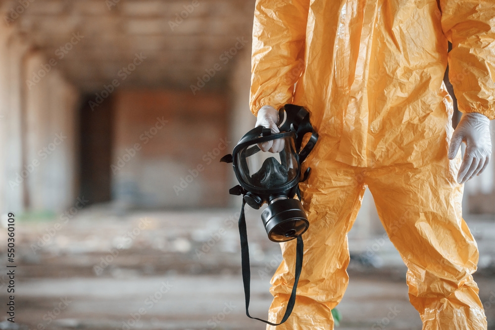 Holding gas mask. Man dressed in chemical protection suit in the ruins ...