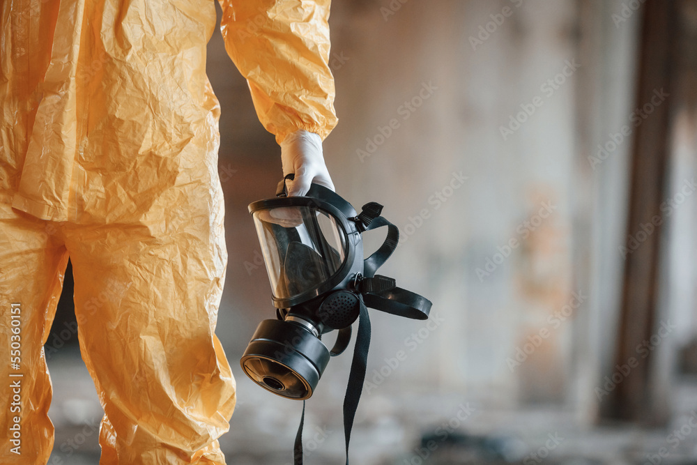 Holding gas mask. Man dressed in chemical protection suit in the ruins ...