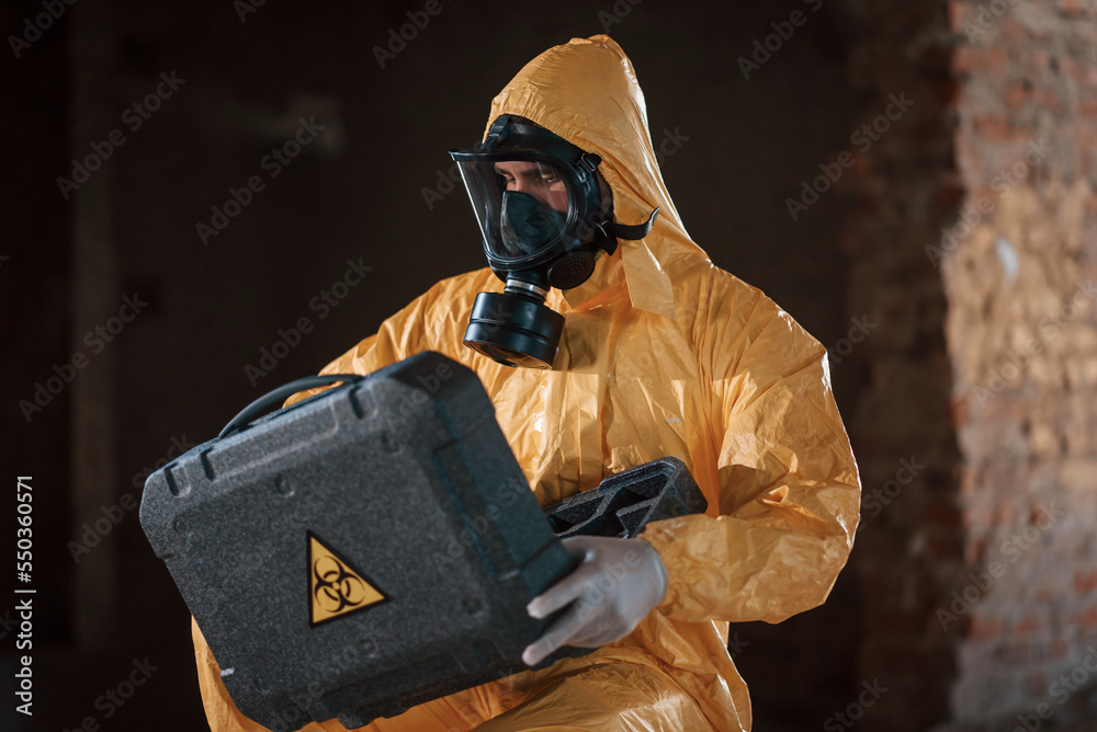 Sitting with radioactive case. Man dressed in chemical protection suit ...