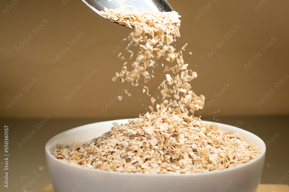 Avena molida siendo vertida en un bol blanco con una cuchara de metal ...