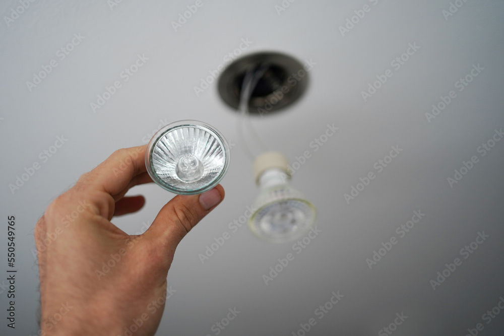 Hand holding a new efficient LED spotlight replacing an old one on a ...
