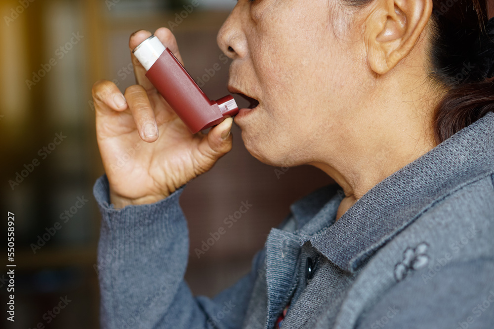 Closeup female senior patient uses brown asthma inhaler for relief ...