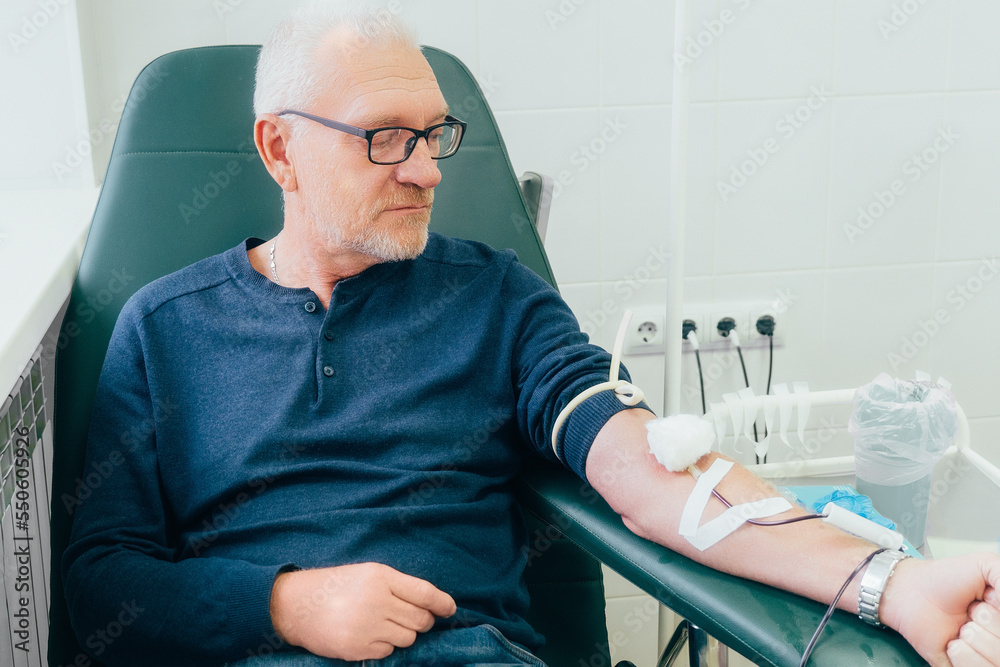 Donor donates blood. Elderly man of 50-60 years old in glasses sits in ...