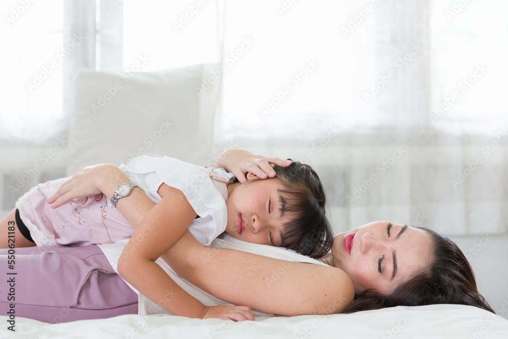 Child little girl sleep on mother's on bed at home. Mother take care her Asian daughter with ...