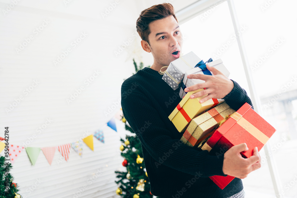 Portrait of an excited and surprised young Asian man holding many gifts ...