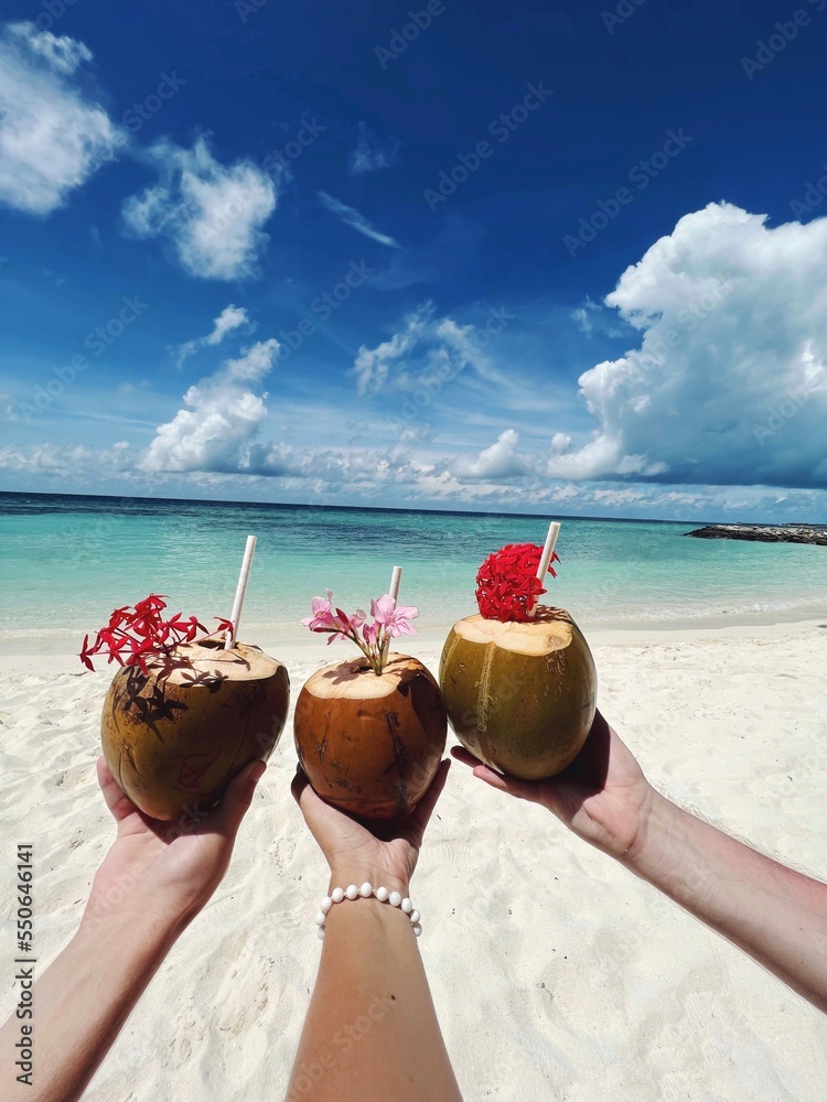 Tropical coconut cocktails in the hands of three people on the beach of ...
