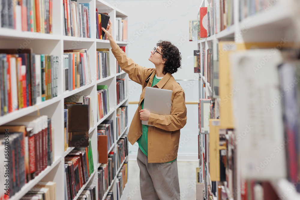 young beautiful woman with curly hair in the library among the shelves ...