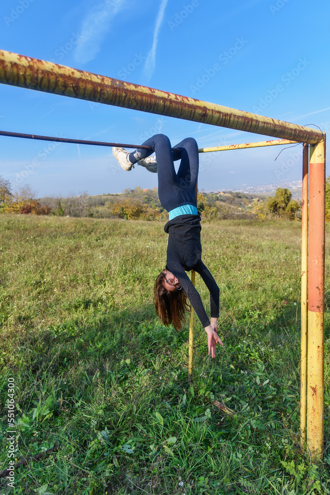 The girl is hanging by her feet on the pole. Girl doing pull-ups with her legs. Girl hanging ...