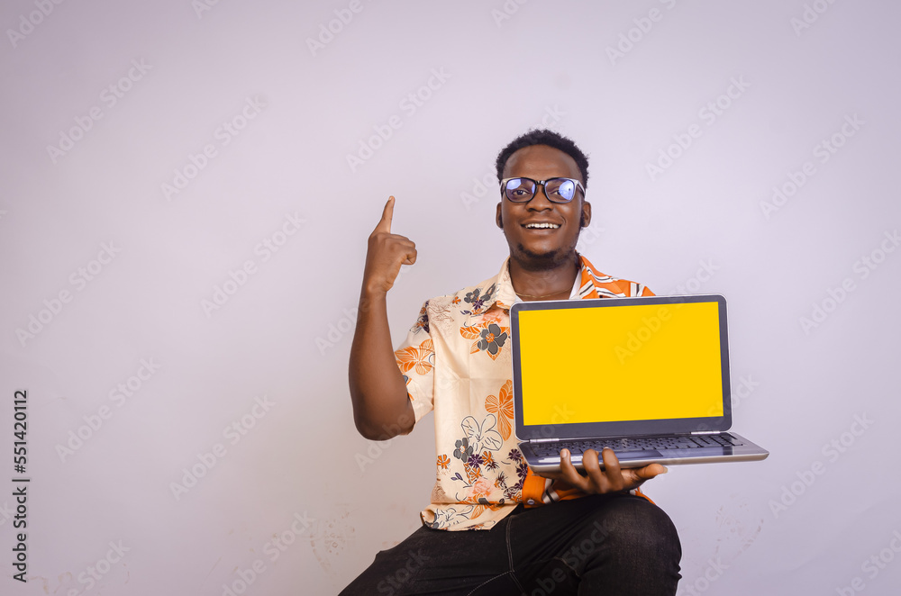 Handsome young black African male sitting and holding laptop smiling ...