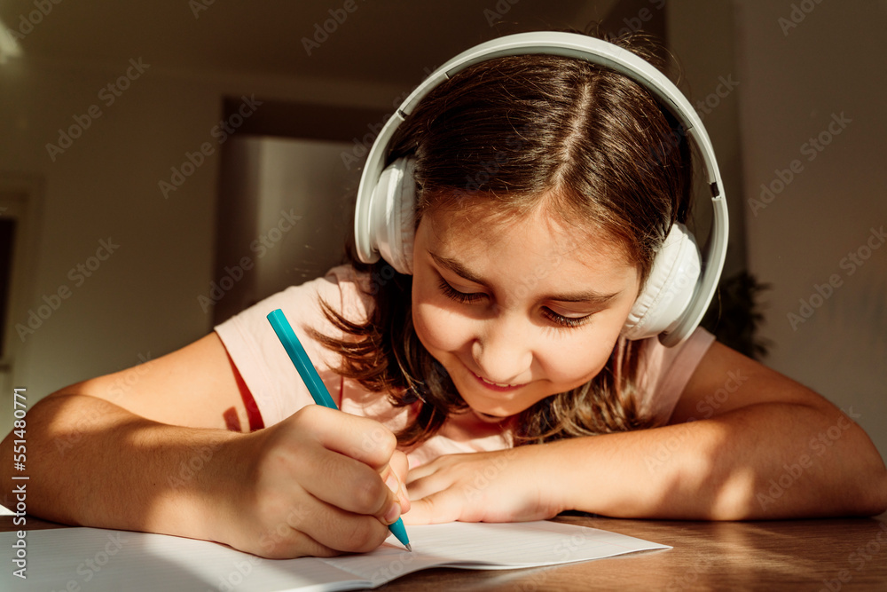 Smiling girl wearing wireless headphones writing in book at desk Stock ...