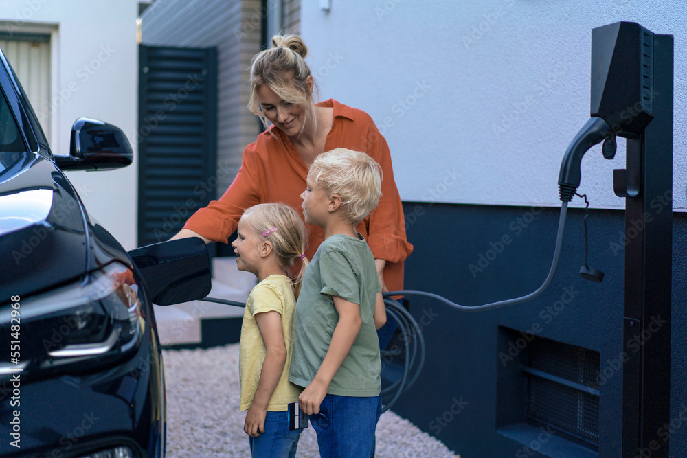 Smiling mother charging electric car by children in front yard Stock ...