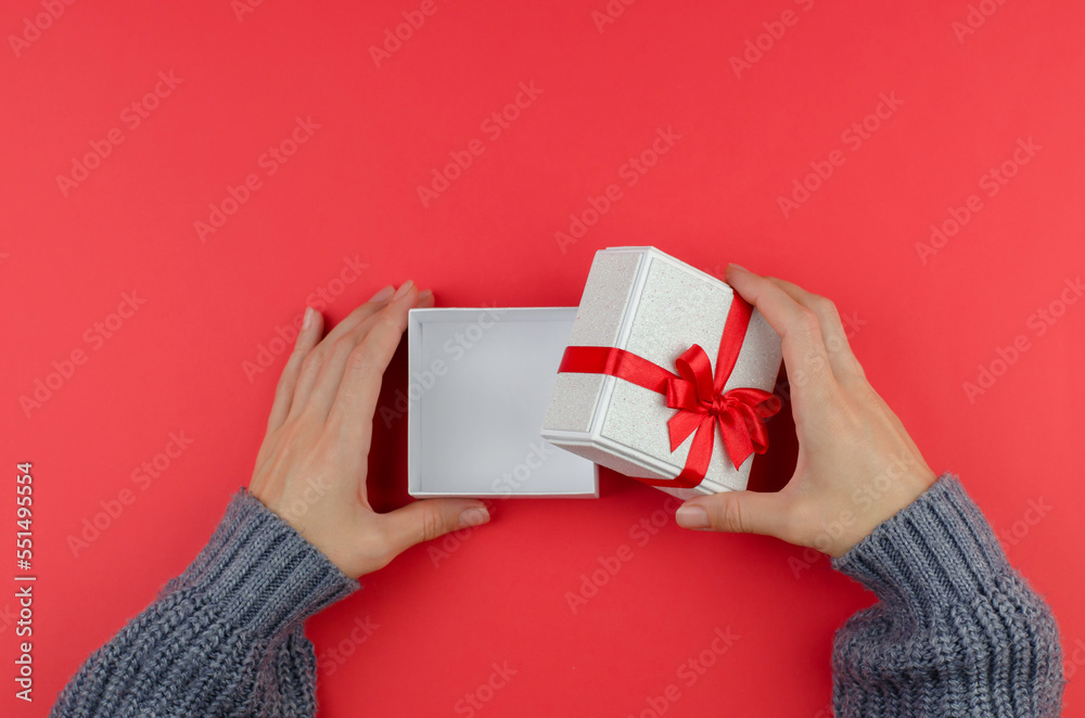 Open gift box in female hands on a red background. Woman opening a ...