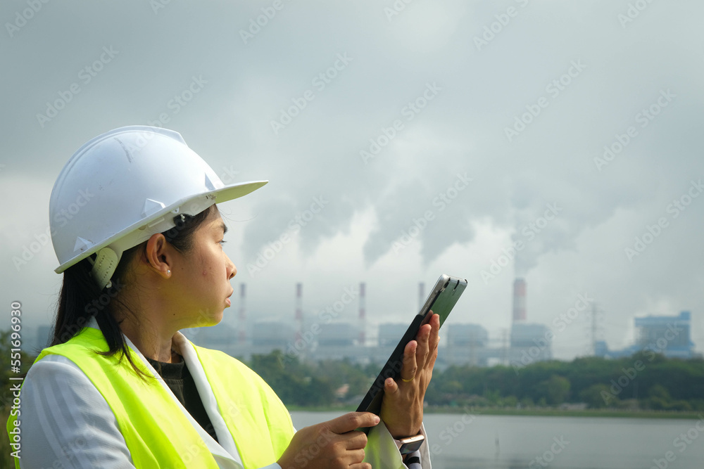Female chief engineer wearing a green vest and helmet stands outside ...
