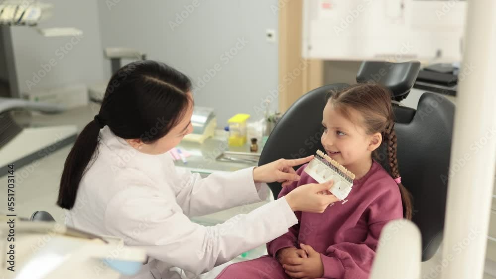 Asian dentist checking and selecting color of young caucasian girl's ...