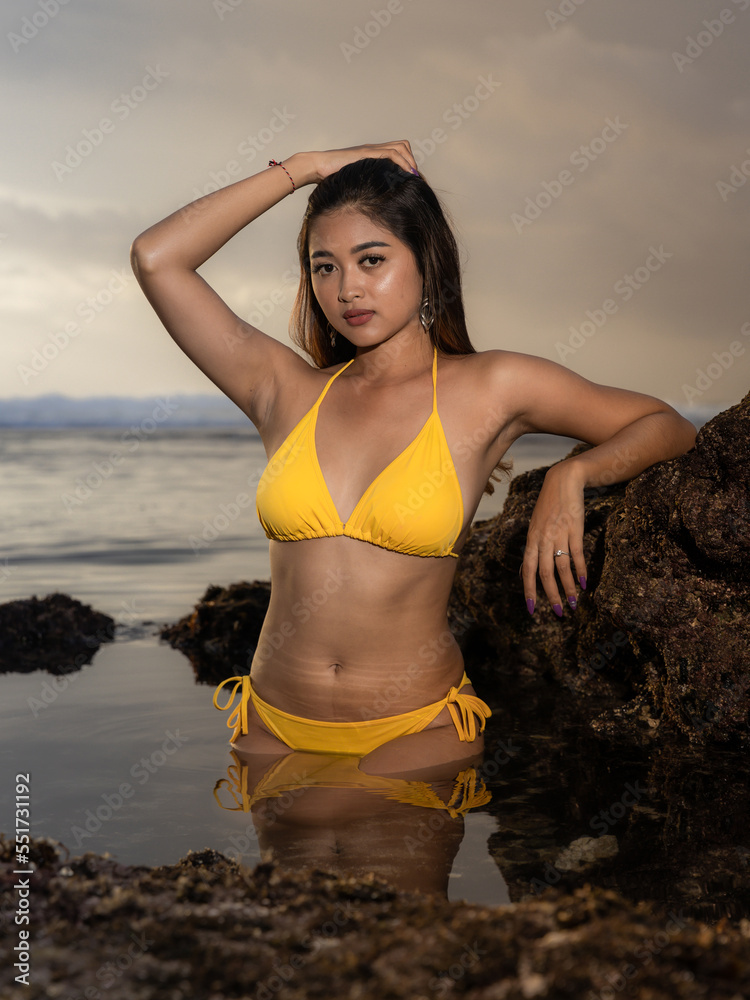 Foto de Sexy Asian woman spending sunset on the beach. Attractive woman wearing yellow bikini ...