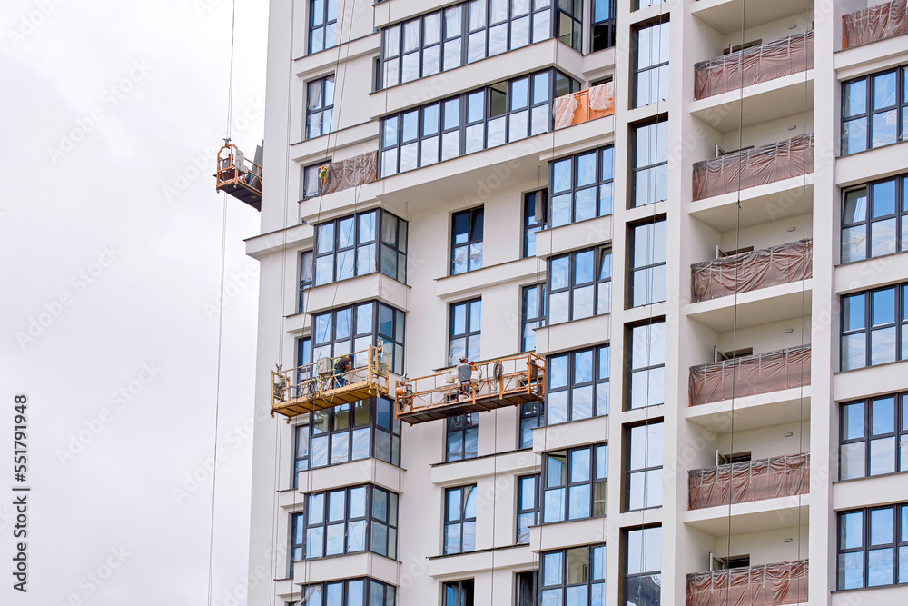 Workers in lift platform caulk, seal exterior glass window, maintain ...