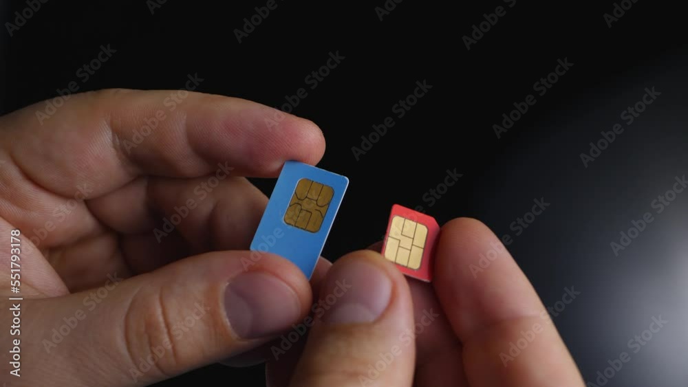 Blue mini-SIM card and red micro-SIM card in male's hand on black ...