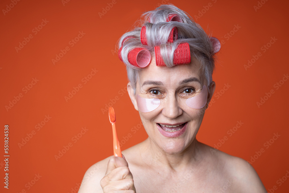 portrait of a cute elderly grandmother with curlers who brushes her ...