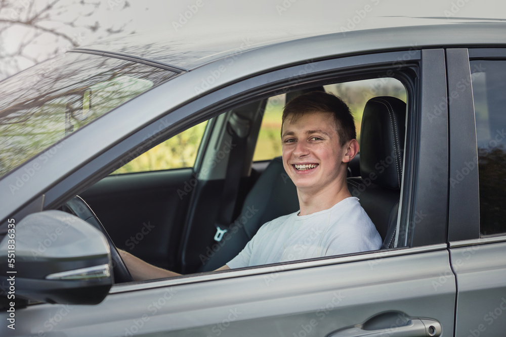 Joyful young man driving safe his new car, looking cheerful to camera ...