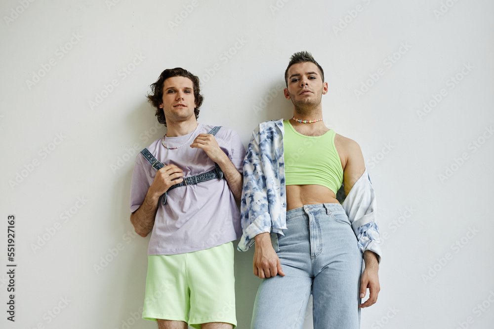 Portrait of two non binary men wearing pastel colored outfits with crop tops against white in ...