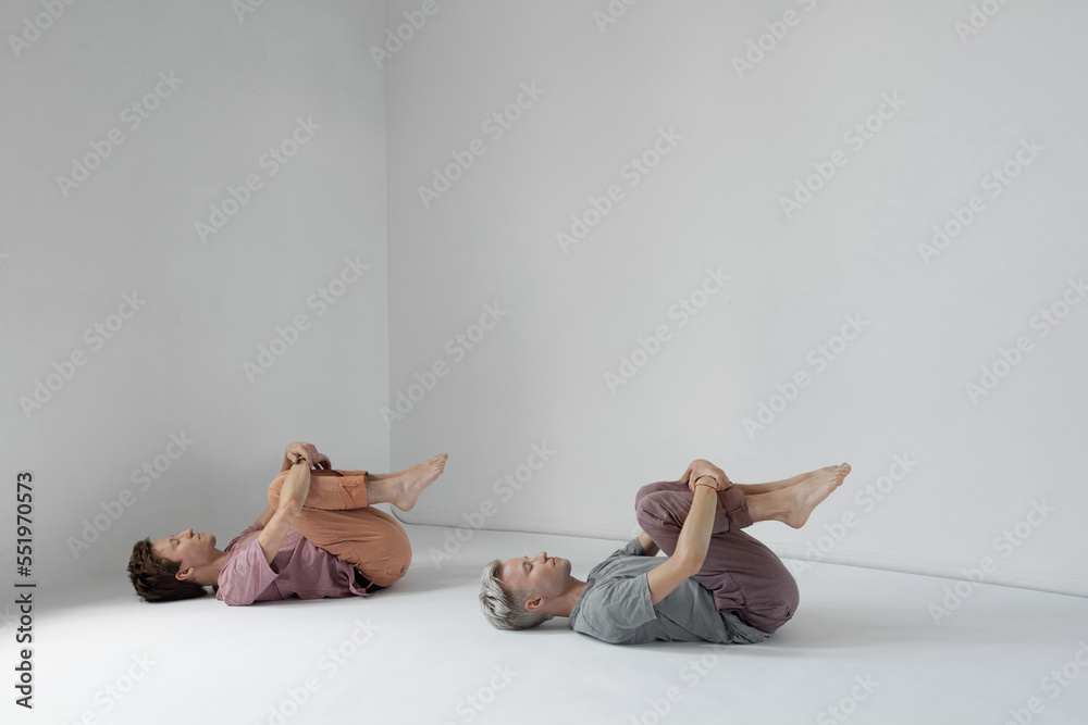Horizontal shot of two young men lying on floor in identical poses with ...