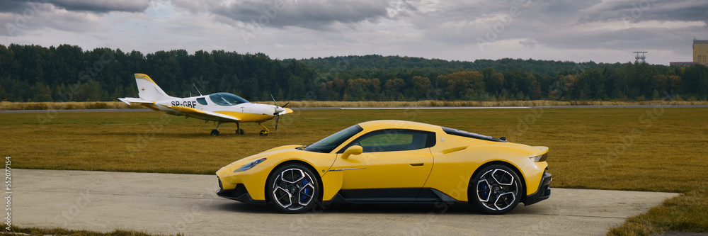 Yellow Maserati MC20 parked at the airport. A small light aircraft in ...