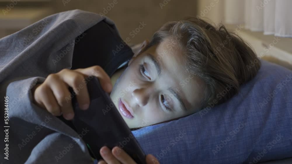 Phone addicted boy playing on the phone at night in bed. The boy lying ...