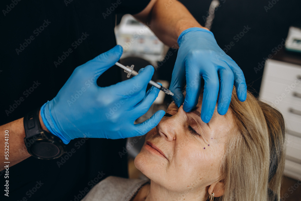 Plastic surgeon in protective gloves injecting face filler to senior ...
