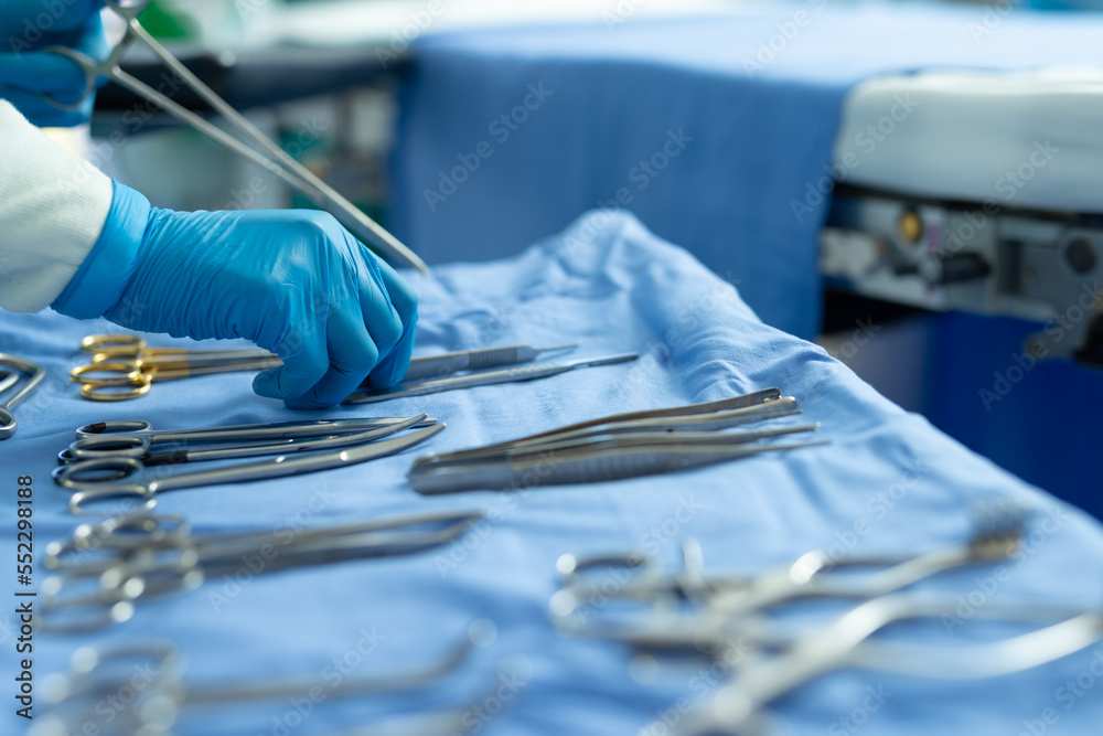 Gloved hand of surgical tech placing tools on table in operating ...
