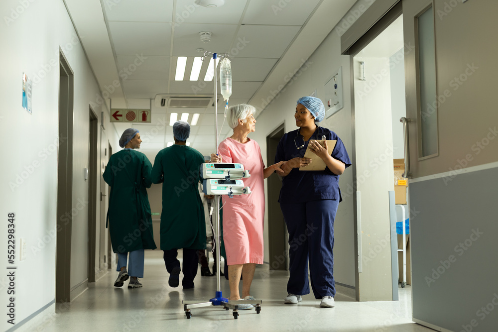Happy diverse female doctor and senior female patient with iv pole ...