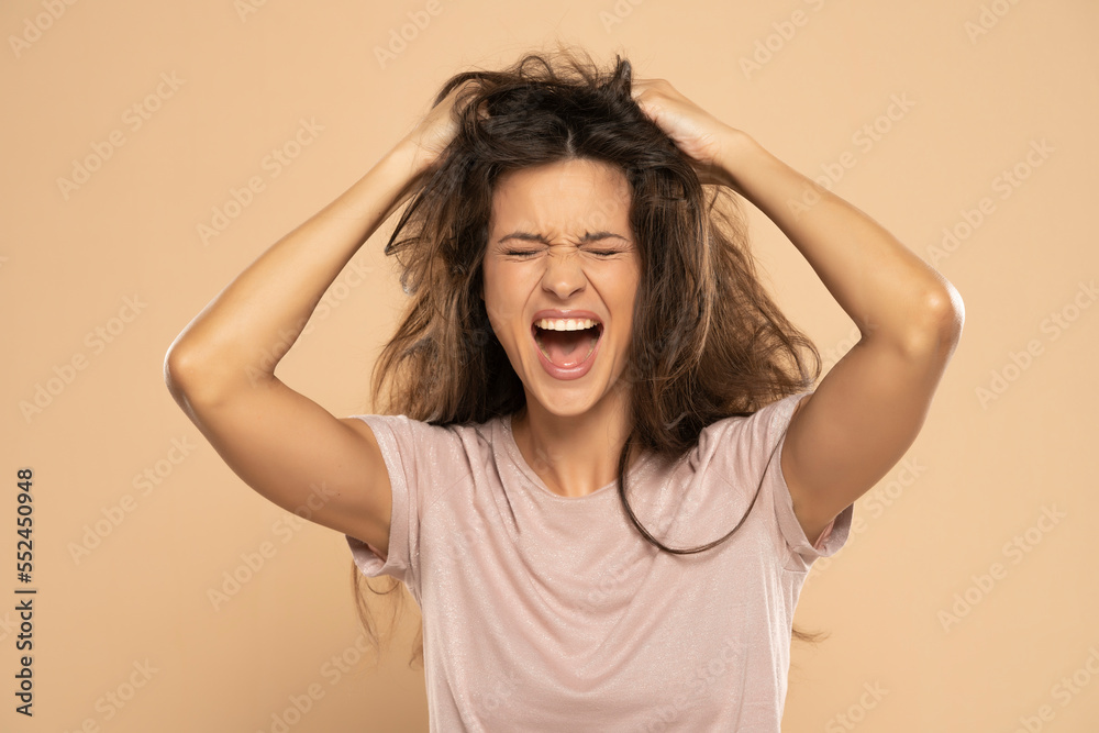 Angry nervous woman pulling her messy long hair on a beige background ...
