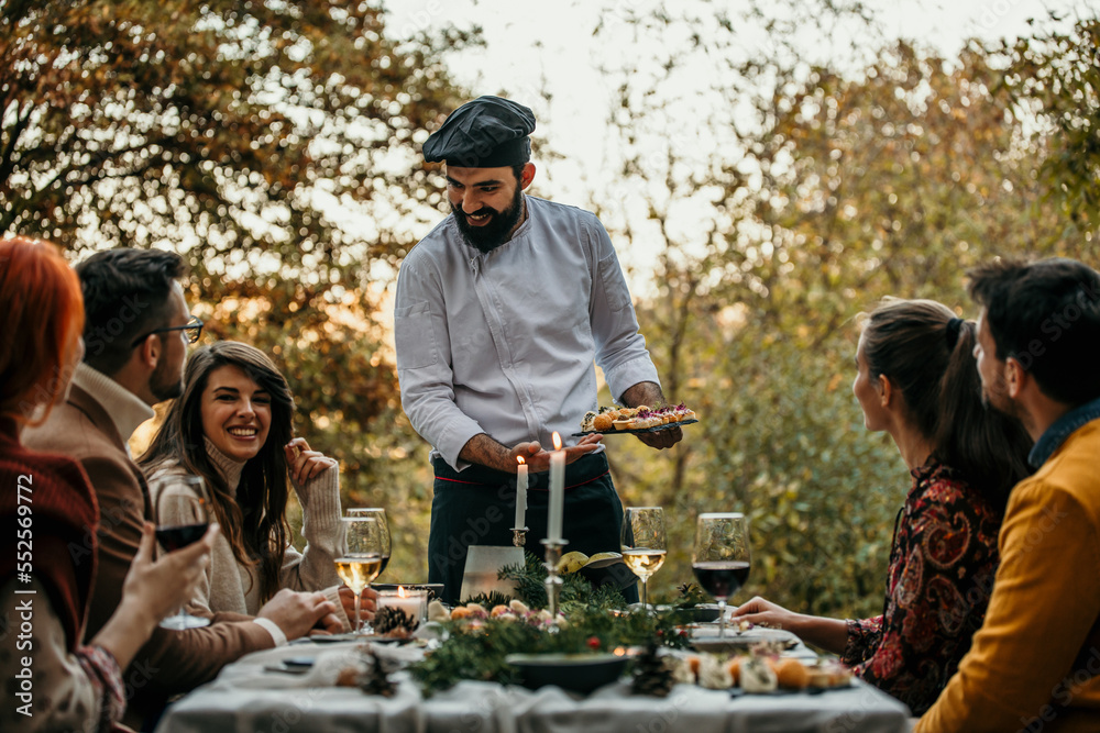 A male chef in uniform is serving a private elegant dinner to a group ...