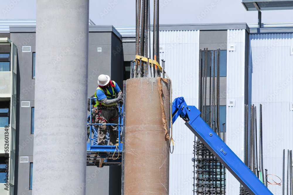 Workers on an aerial lift work on a concrete column at a construction ...
