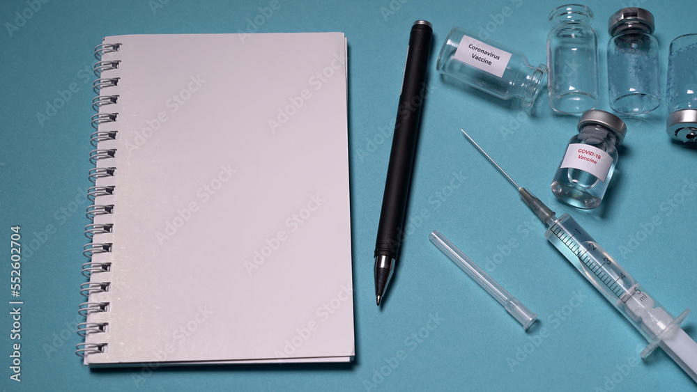 Blank notebook with pen on a blue background. Empty vaccine vials and a ...