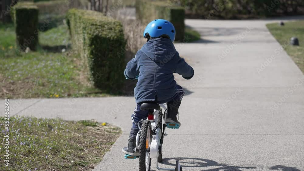 Back of child riding bicycle outdoors wearing helmet. One little boy ...