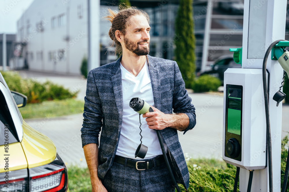 Businessman holding charging pistol while charging car at electric ...