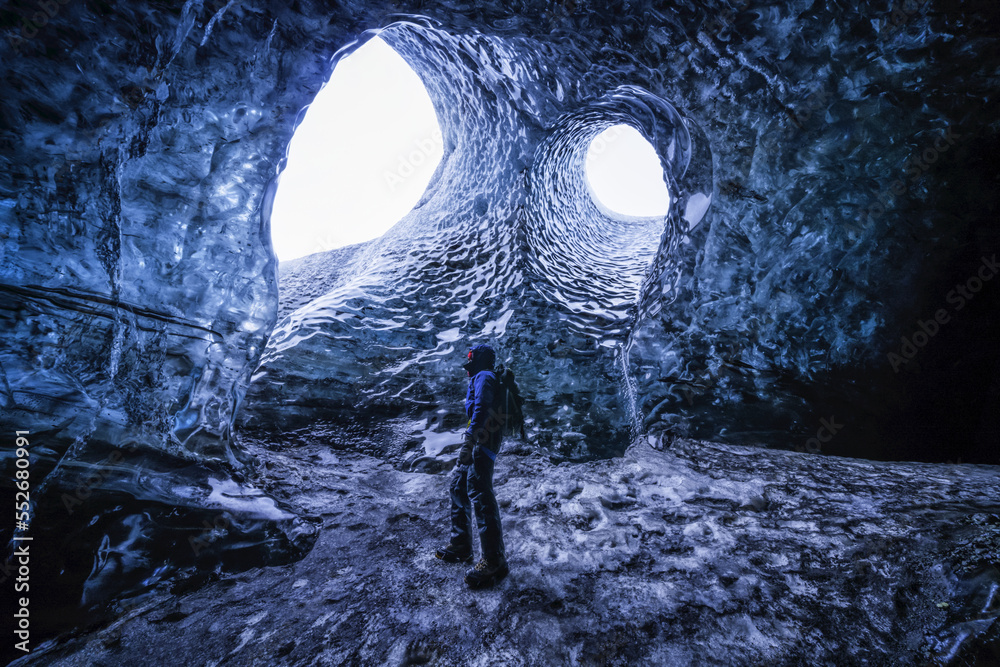 Person standing underneath the openings of a glacier, South Iceland ...
