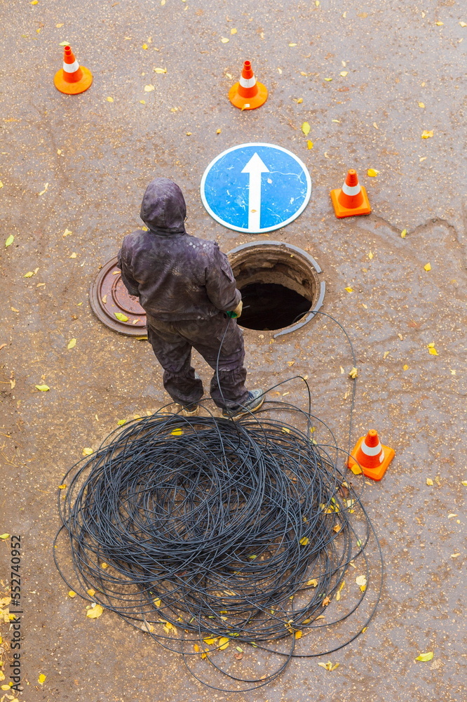 signalman worker pulling an electric cable through the city well, top ...