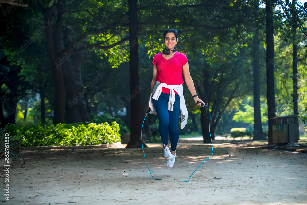 young Indian woman with jump rope and doing skipping workout in a park ...