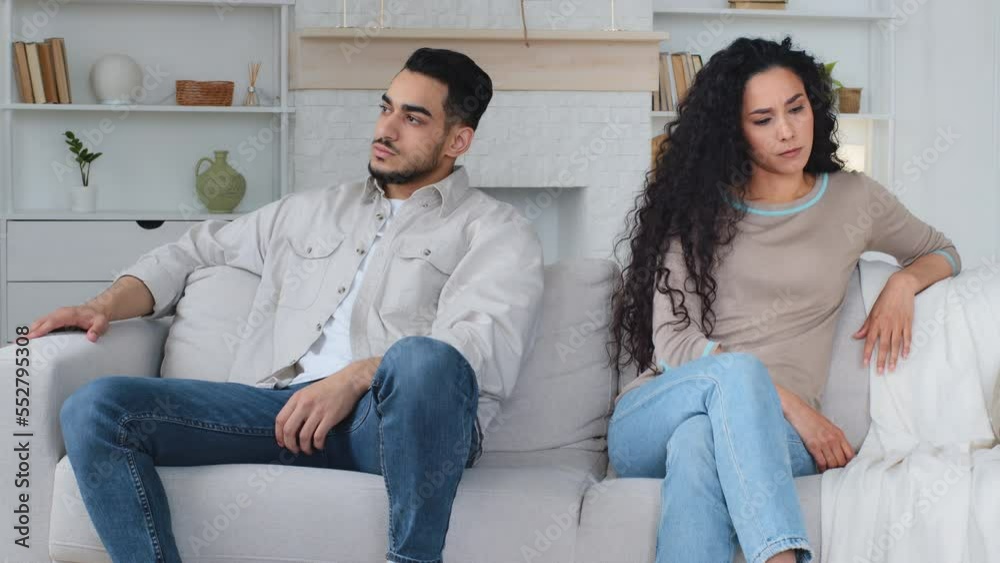Angry Hispanic Indian man husband sitting on sofa separately from sad ...